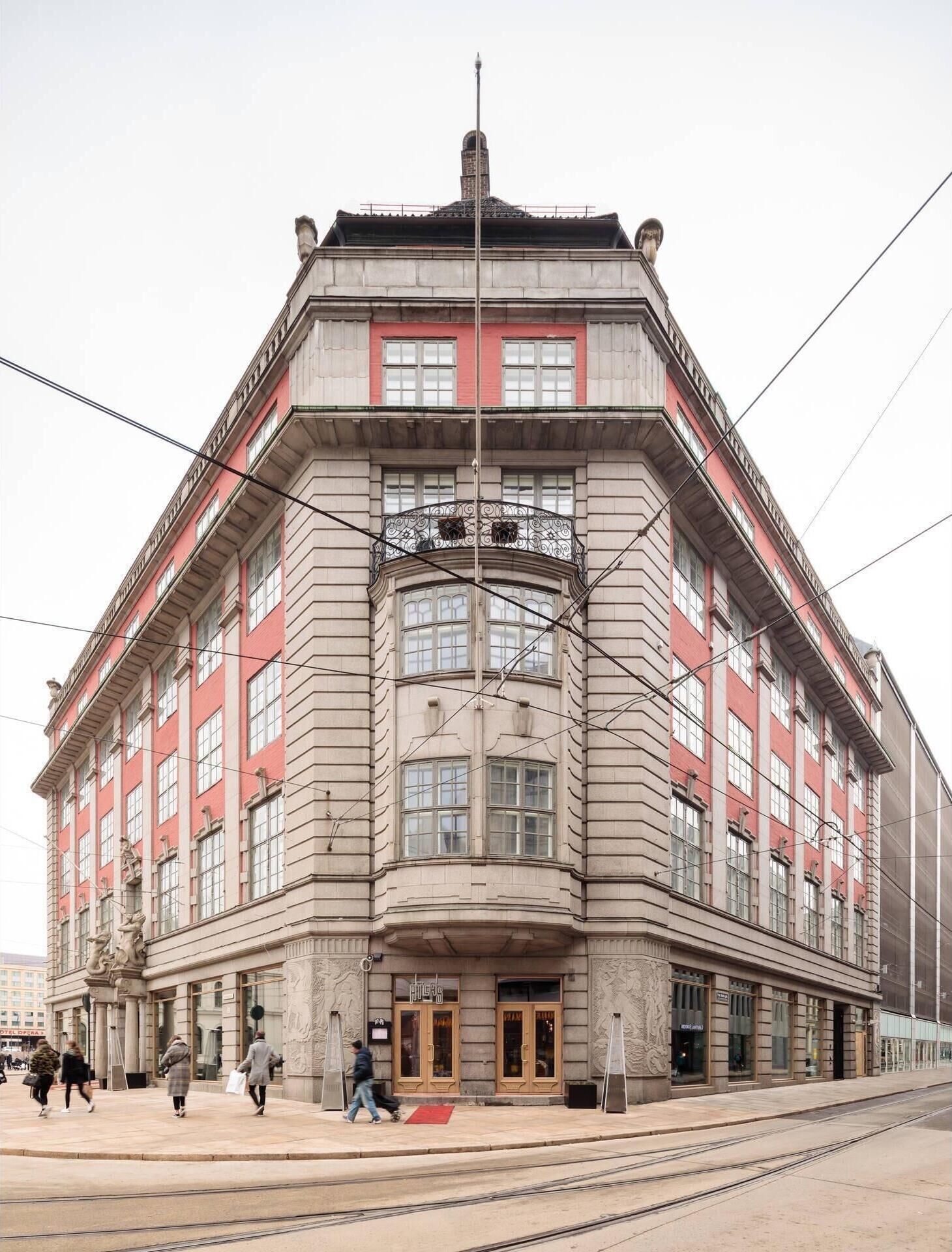 Um edifício em esquina com entrada imponente, grandes janelas e uma varanda com grades ornamentadas.