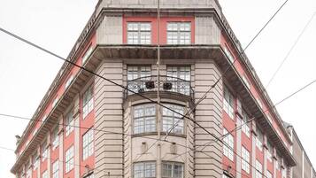 Um edifício em esquina com entrada imponente, grandes janelas e uma varanda com grades ornamentadas.