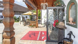 Uma entrada de madeira com um tapete vermelho, um portão de metal com um vaso de flores decorativo e uma bomba de água de pedra.