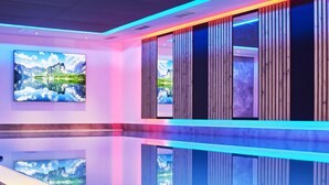 Área interna de piscina moderna com painéis de madeira e grandes telas digitais exibindo paisagens.