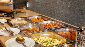 Buffet com diversas opções de comida, incluindo ovos, bacon e ovos mexidos.