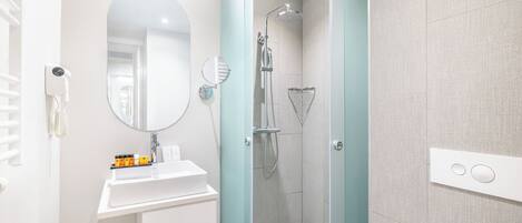 Uma casa de banho moderna com uma pia branca, um espelho redondo, um chuveiro manual e uma cabine de duche com paredes de vidro.