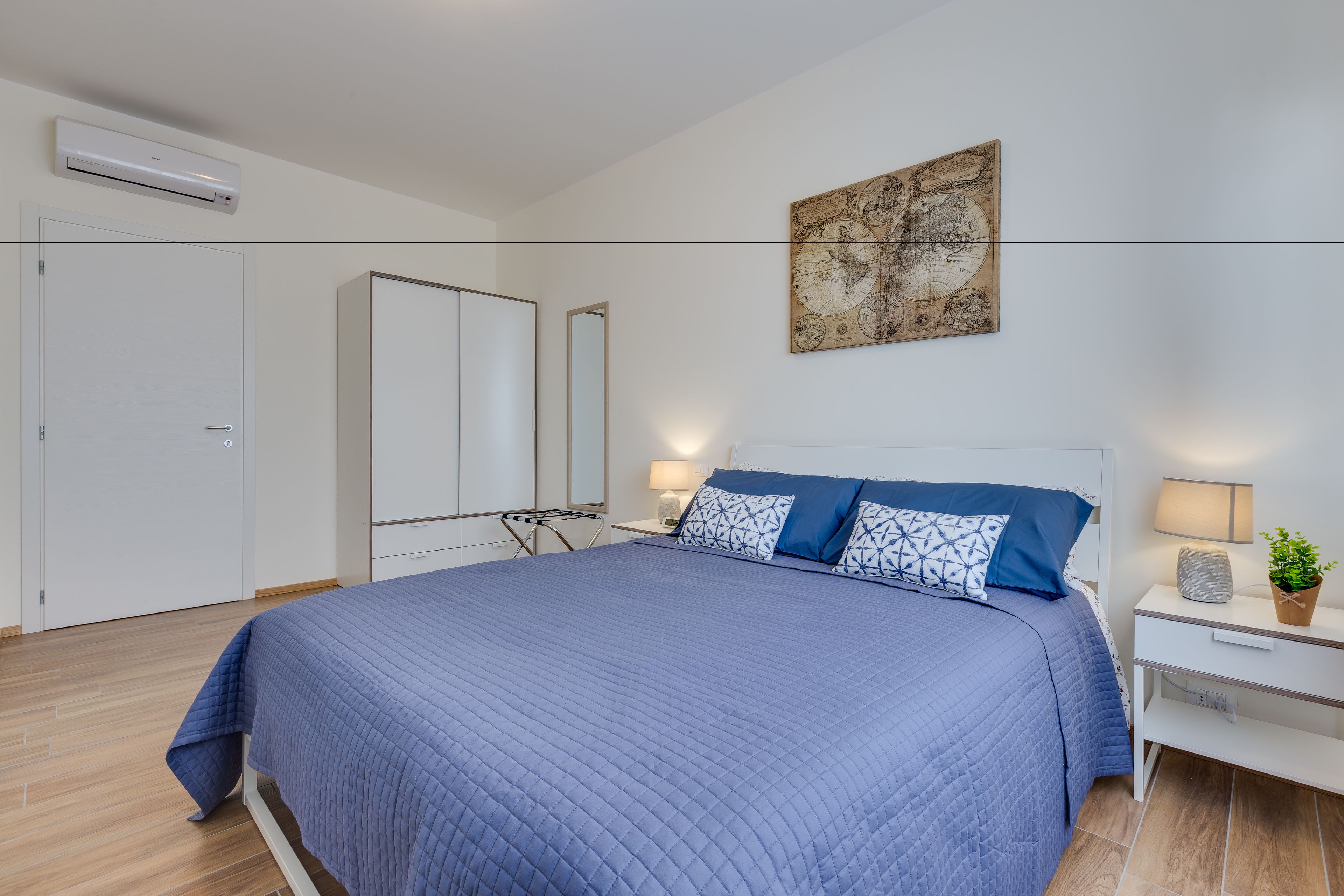 Quarto com uma cama grande, mesa de cabeceira, ar condicionado fixado na parede, guarda-roupa e uma obra de arte com um mapa na parede.