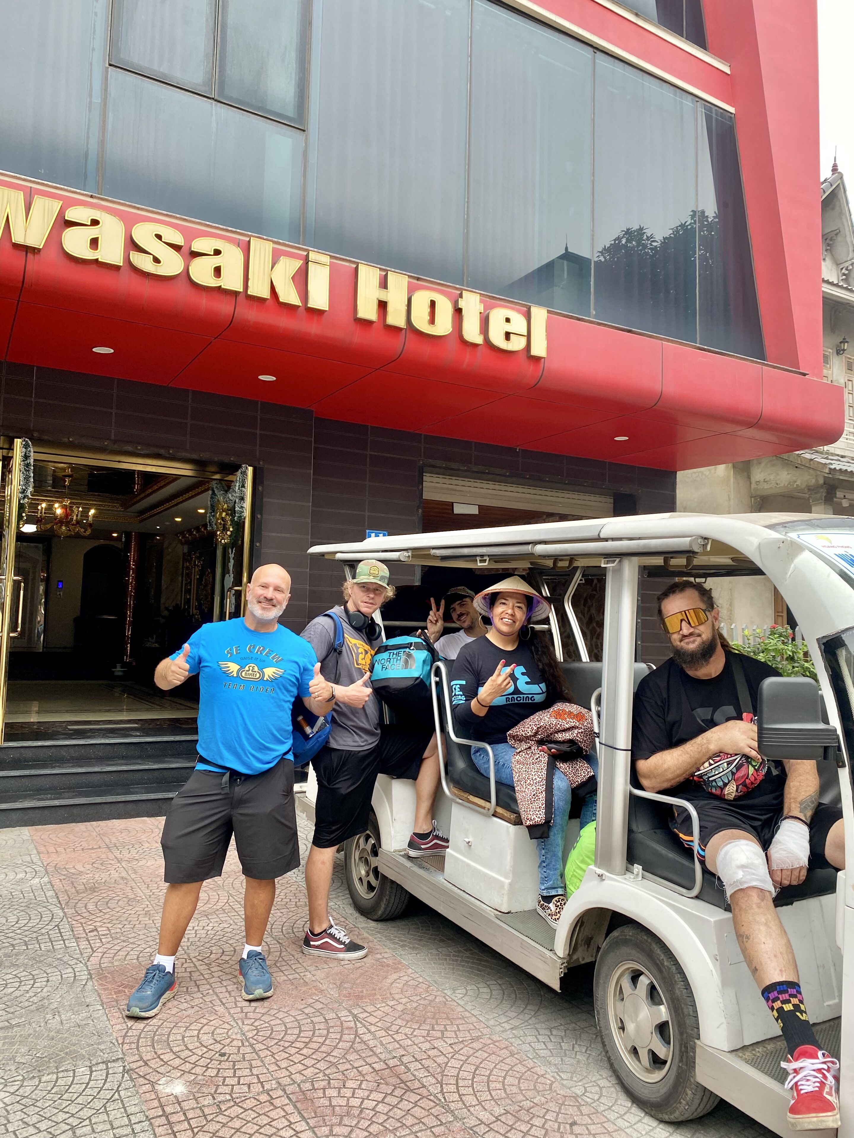 Um grupo de pessoas em frente a um prédio com uma placa que diz 'Wasaki Hotel'.