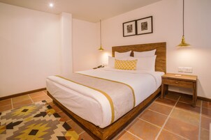 Uma cama bem arrumada com cabeceira de madeira, uma mesa de cabeceira com abajur e um tapete estampado no chão.