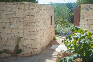 Mural de pedra com uma placa, um caminho e um jardim com flores roxas.
