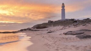 Um farol numa costa rochosa com uma praia e oceano.