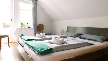 Quarto de hotel com duas camas, uma cadeira, uma mesa com abajur e uma janela com cortinas.