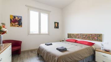 Quarto com cama, escrivaninha, cadeira e obras de arte nas paredes.