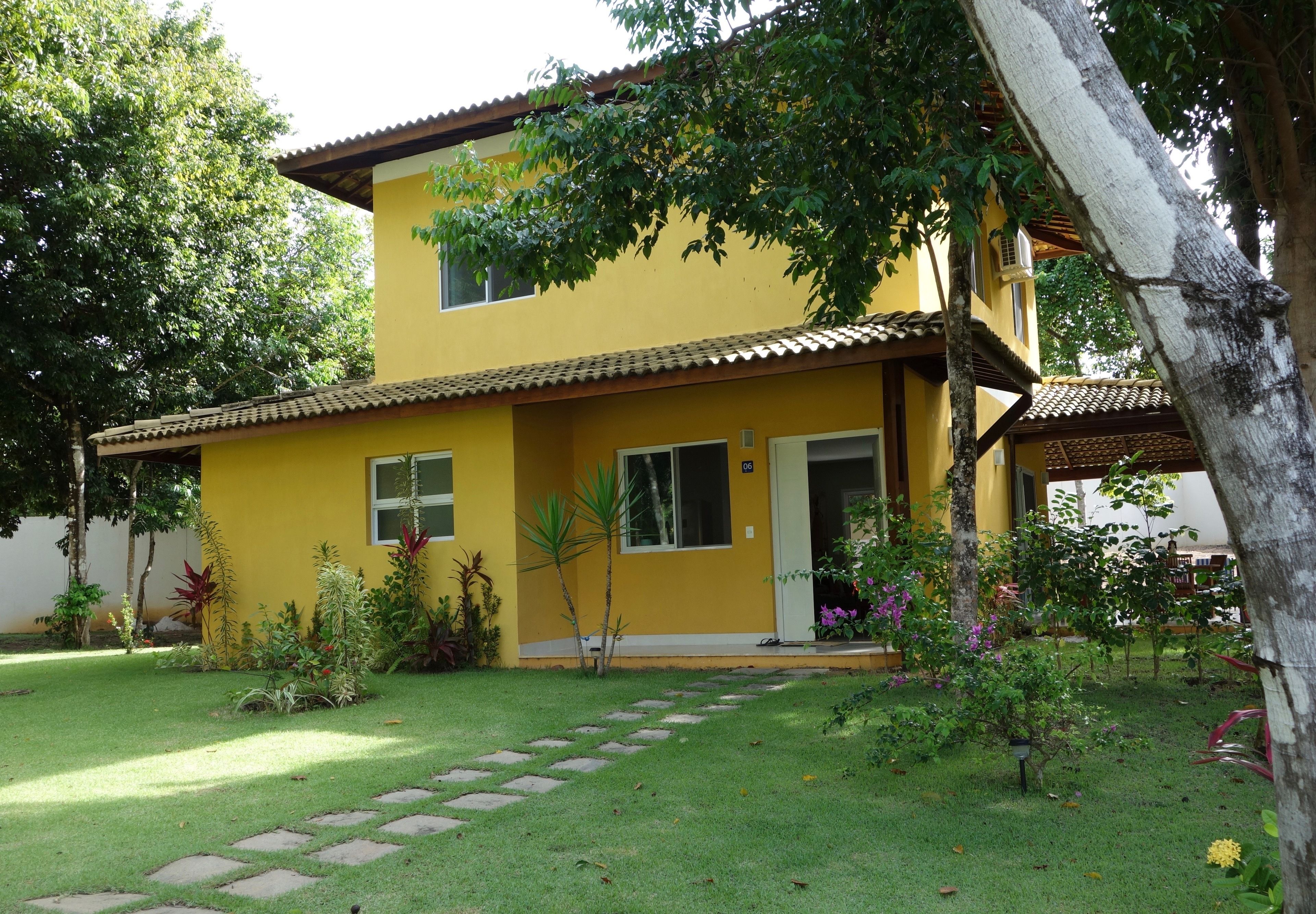 Um edifício amarelo de dois andares com telhado de telhas, porta frontal e pequena varanda.