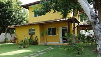 Um edifício amarelo de dois andares com telhado de telhas, porta frontal e pequena varanda.