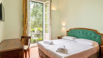 Quarto de hotel com cama, escrivaninha, cadeira, mesa de cabeceira e janela com cortinas.