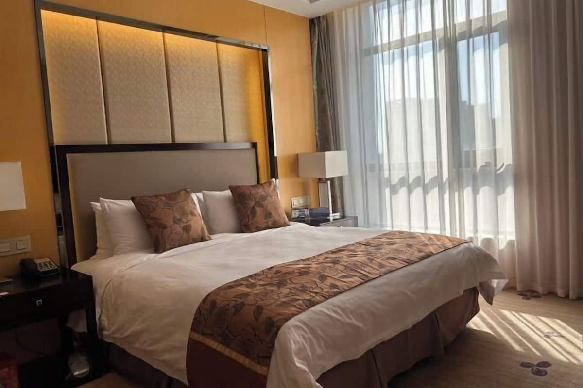 Quarto de hotel com uma cama grande, mesa de cabeceira, abajur e janela com cortinas.