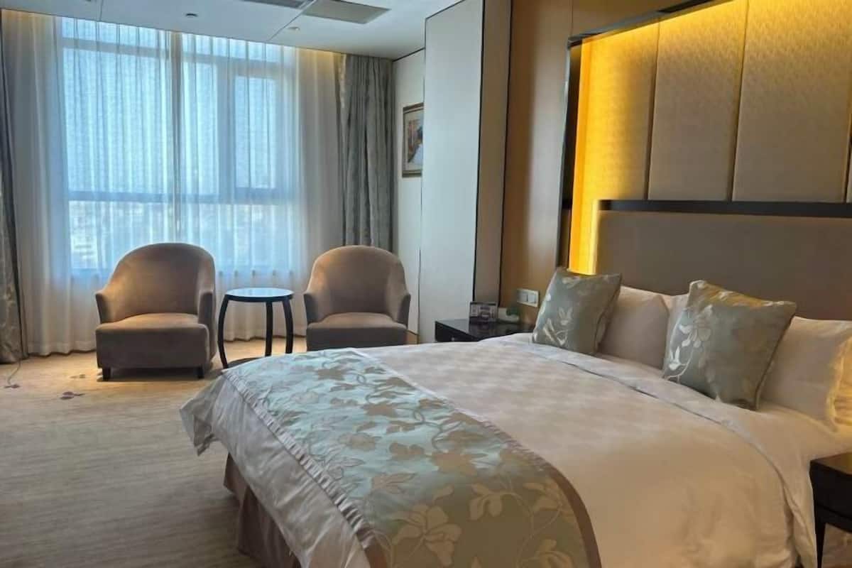 Quarto de hotel com uma cama grande, duas poltronas, uma mesa pequena e uma mesa de cabeceira.