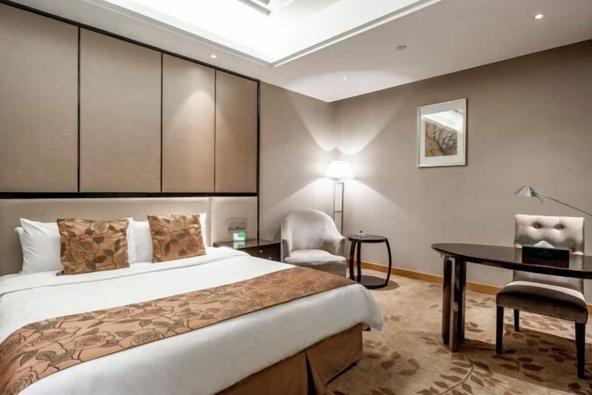 Quarto de hotel com cama, escrivaninha, cadeira, luminária e um quadro na parede.