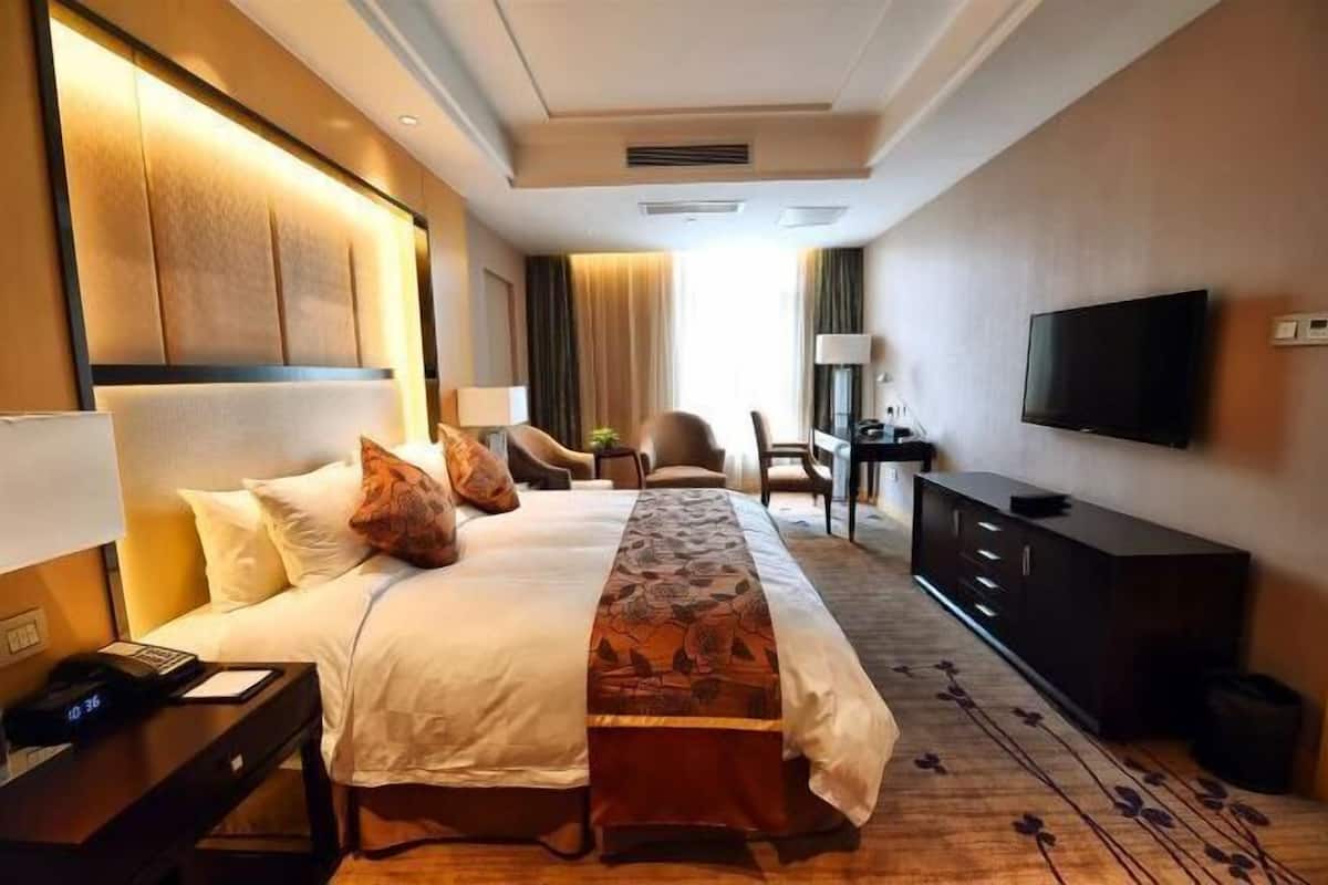 Quarto de hotel com cama, mesa de cabeceira, televisão, escrivaninha, cadeira e uma janela grande.