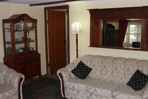 Uma sala de estar com um sofá estampado, um armário de madeira e uma luminária.