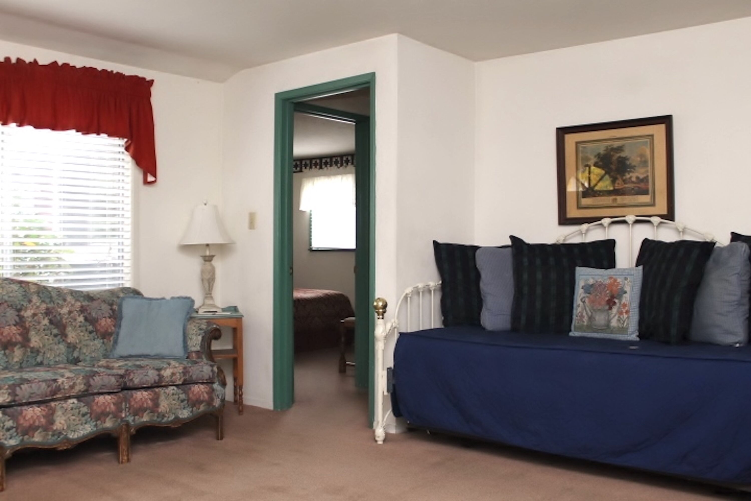 Um quarto com um sofá floral, um sofá azul com almofadas, uma luminária e um quadro na parede.