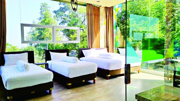 Quarto de hotel com duas camas, janelas amplas e vista para o verde.