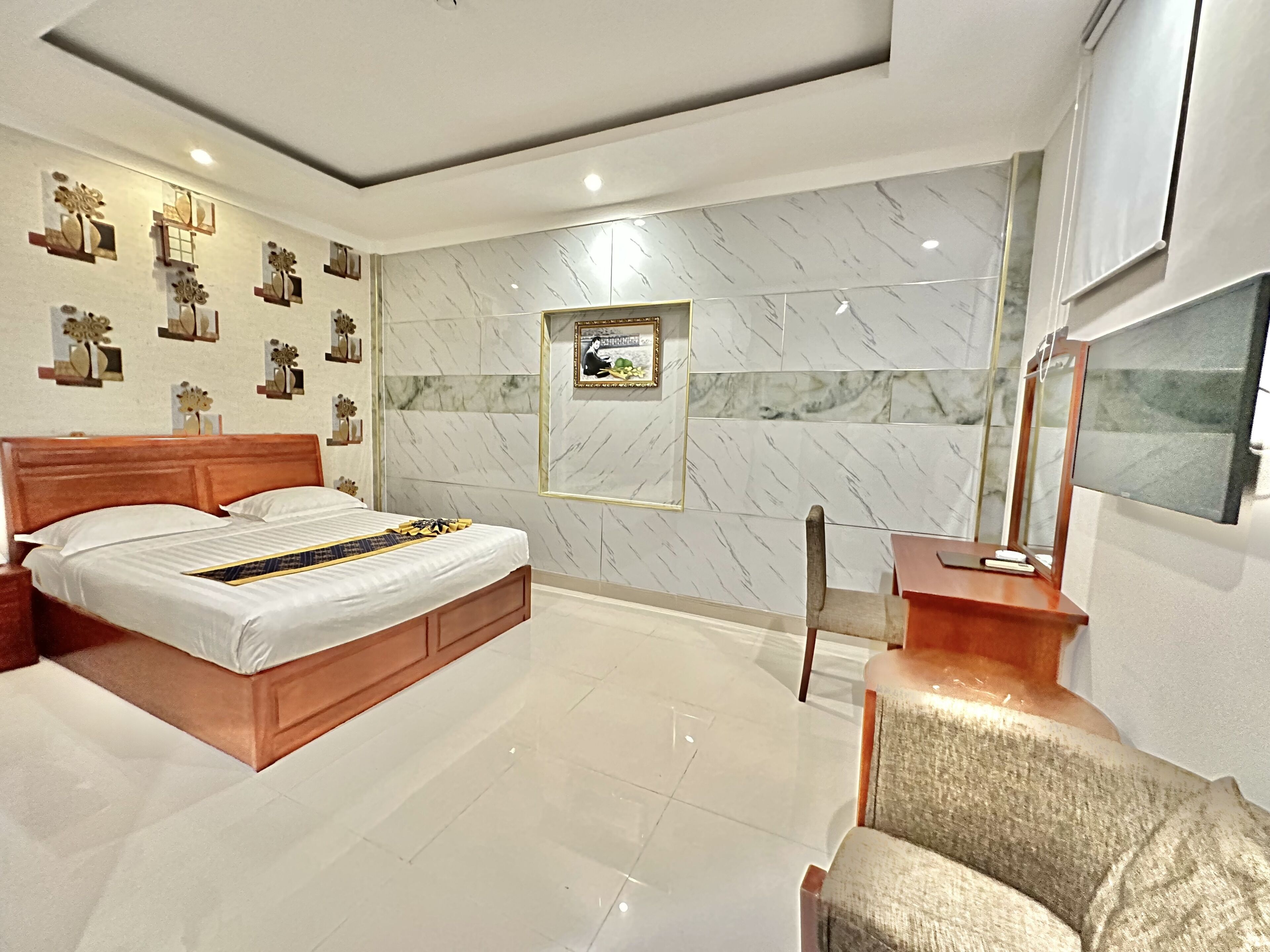 Quarto moderno com uma cama grande, cabeceira de madeira, parede com padrão marmorizado e uma pequena mesa de cabeceira com abajur.