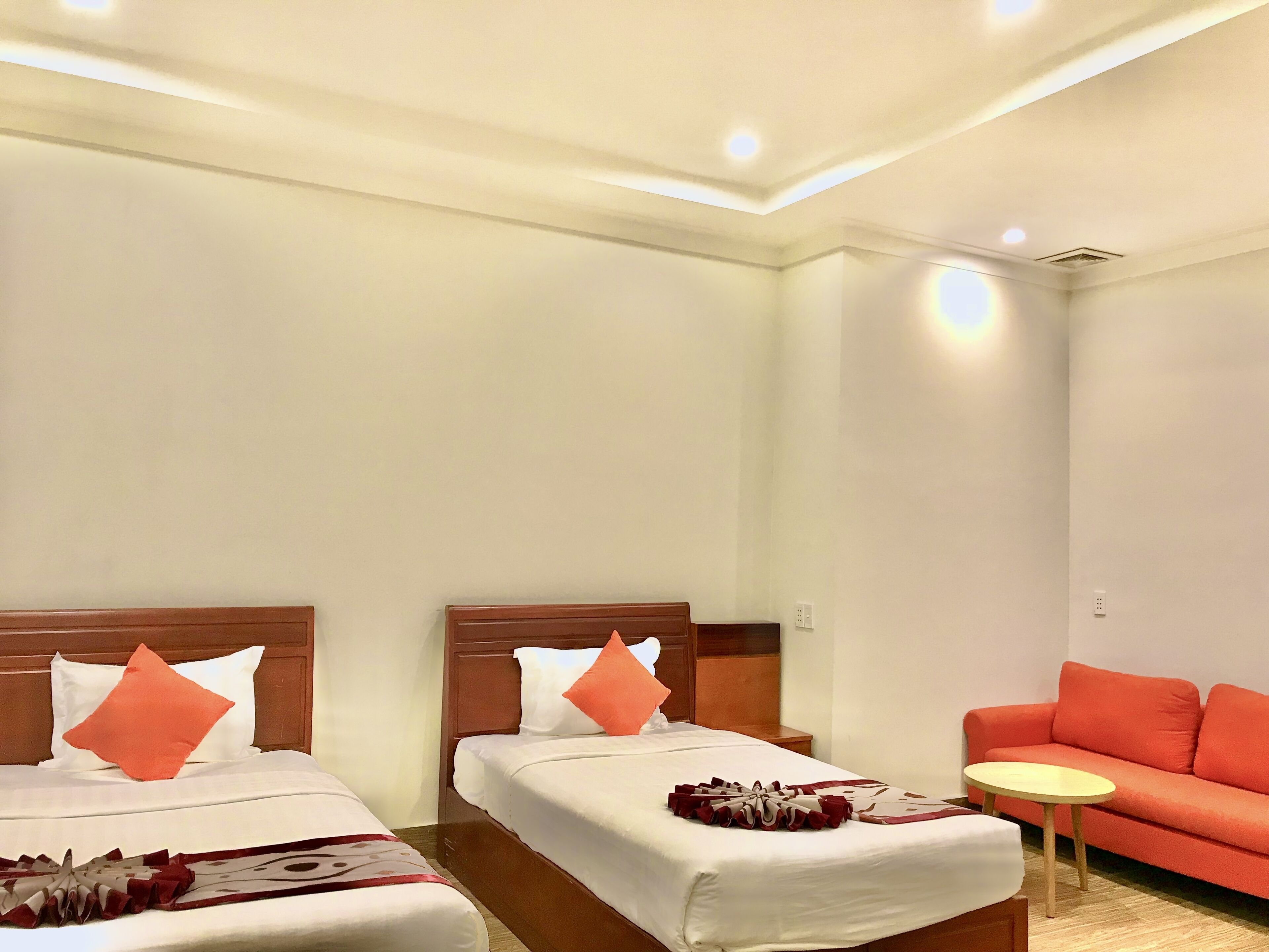Quarto de hotel com duas camas, uma mesinha e um sofá vermelho.