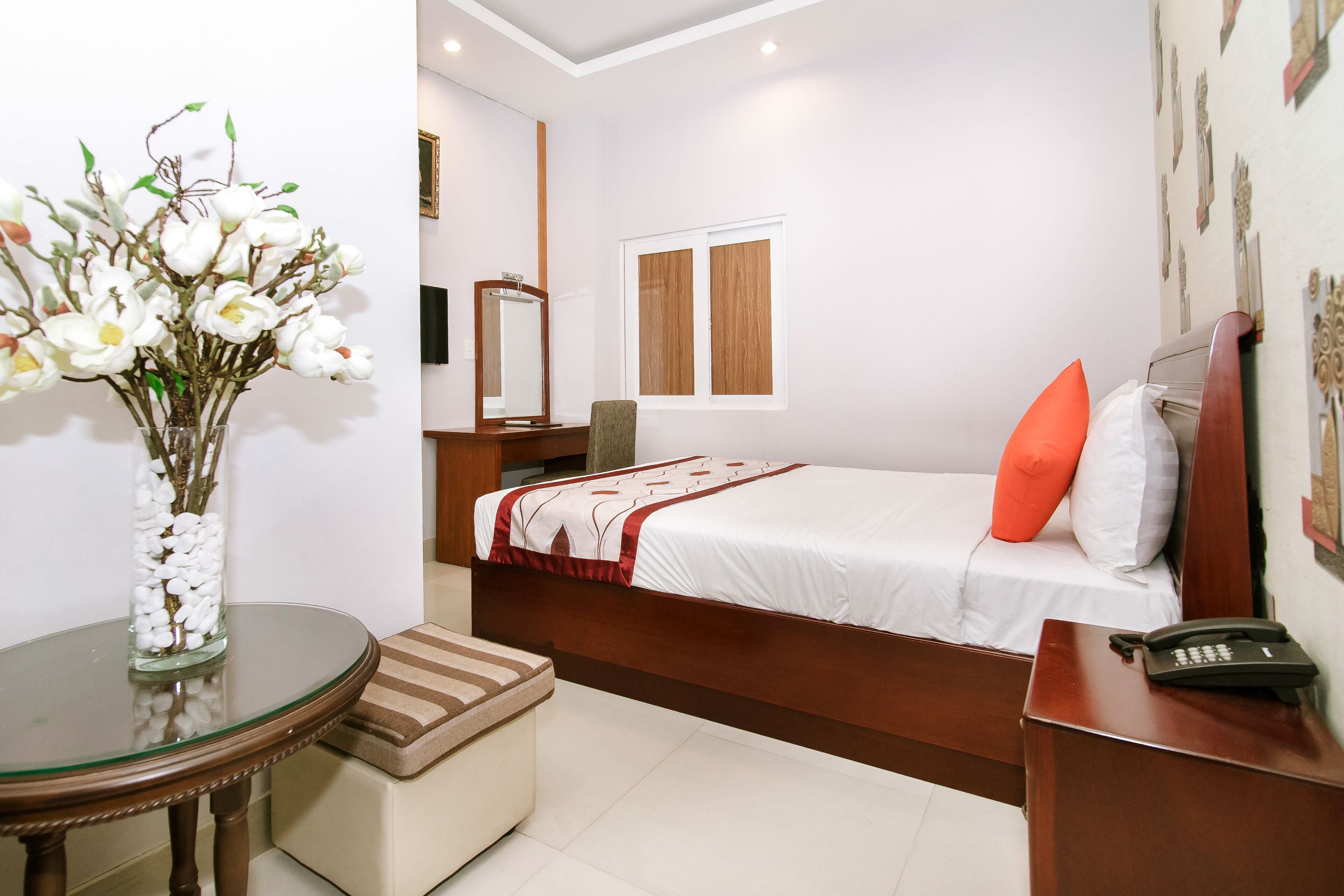 Quarto de hotel com cama, mesa de cabeceira e uma mesa de vidro com um vaso de flores.