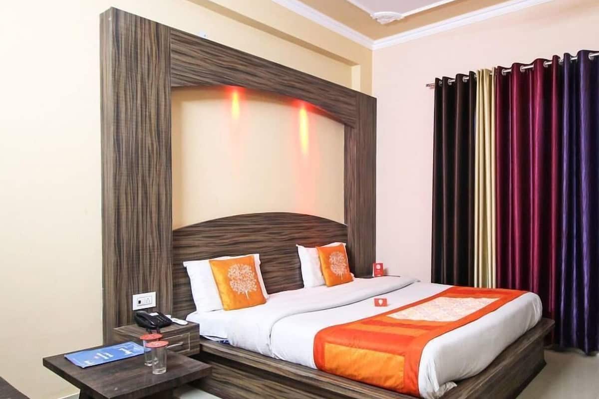 Quarto de hotel com cabeceira de madeira, cama com roupa de cama branca e laranja, mesa de cabeceira com telefone e copo, e um ventilador de teto.