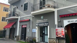 Um edifício com vários andares e varandas, com uma placa indicando 'Constantino Home rooms & apartments' e uma loja 'Relax Art'.