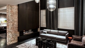 Sala de estar moderna com parede de tijolos, sofá cinza, lareira e uma janela grande com cortinas.