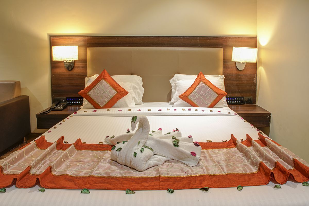 Quarto de hotel com uma cama grande, duas mesas de cabeceira e uma luminária fixada na parede.