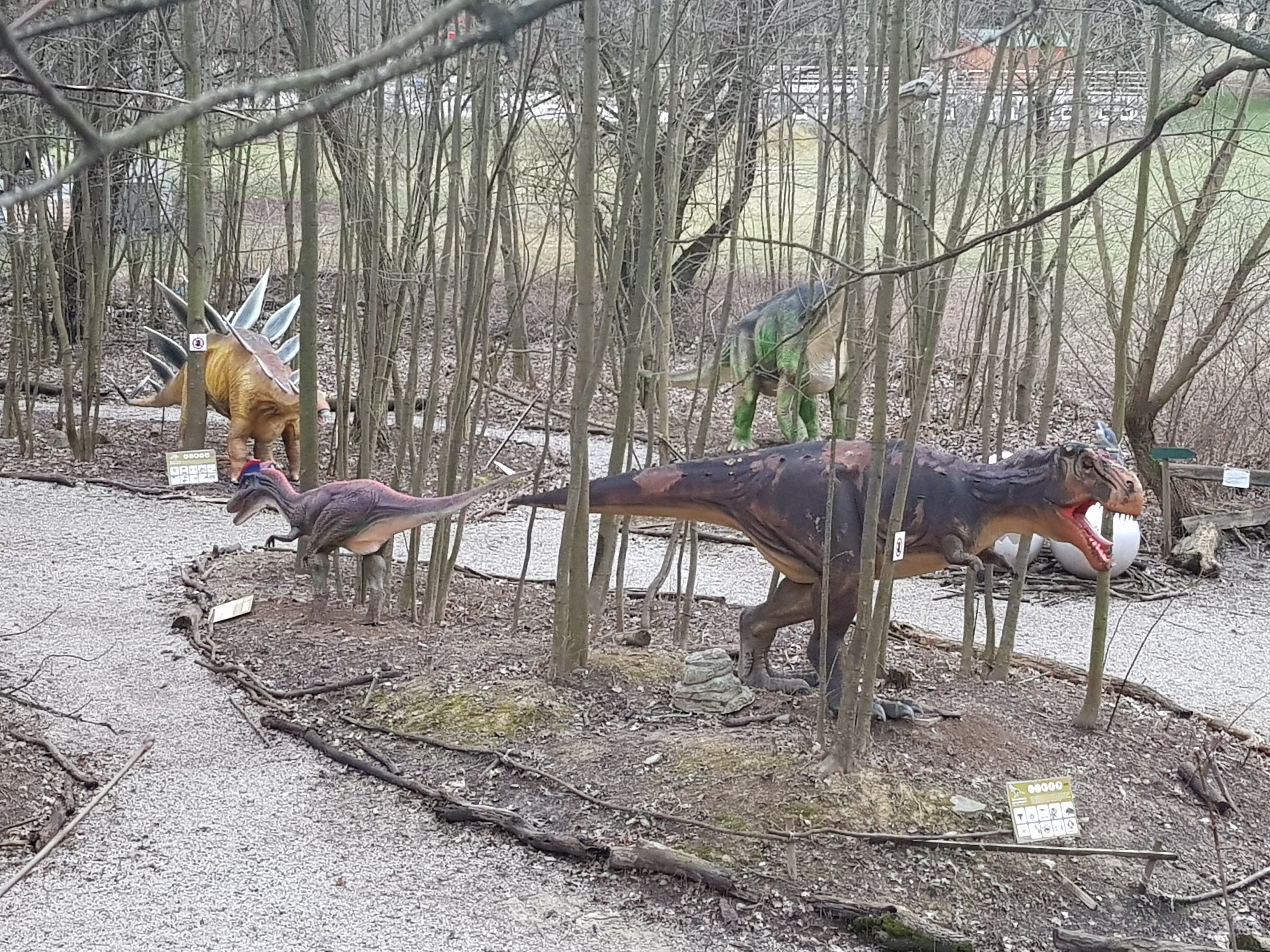 Exposição de dinossauros com diversos modelos exibidos ao ar livre, cercada por árvores.
