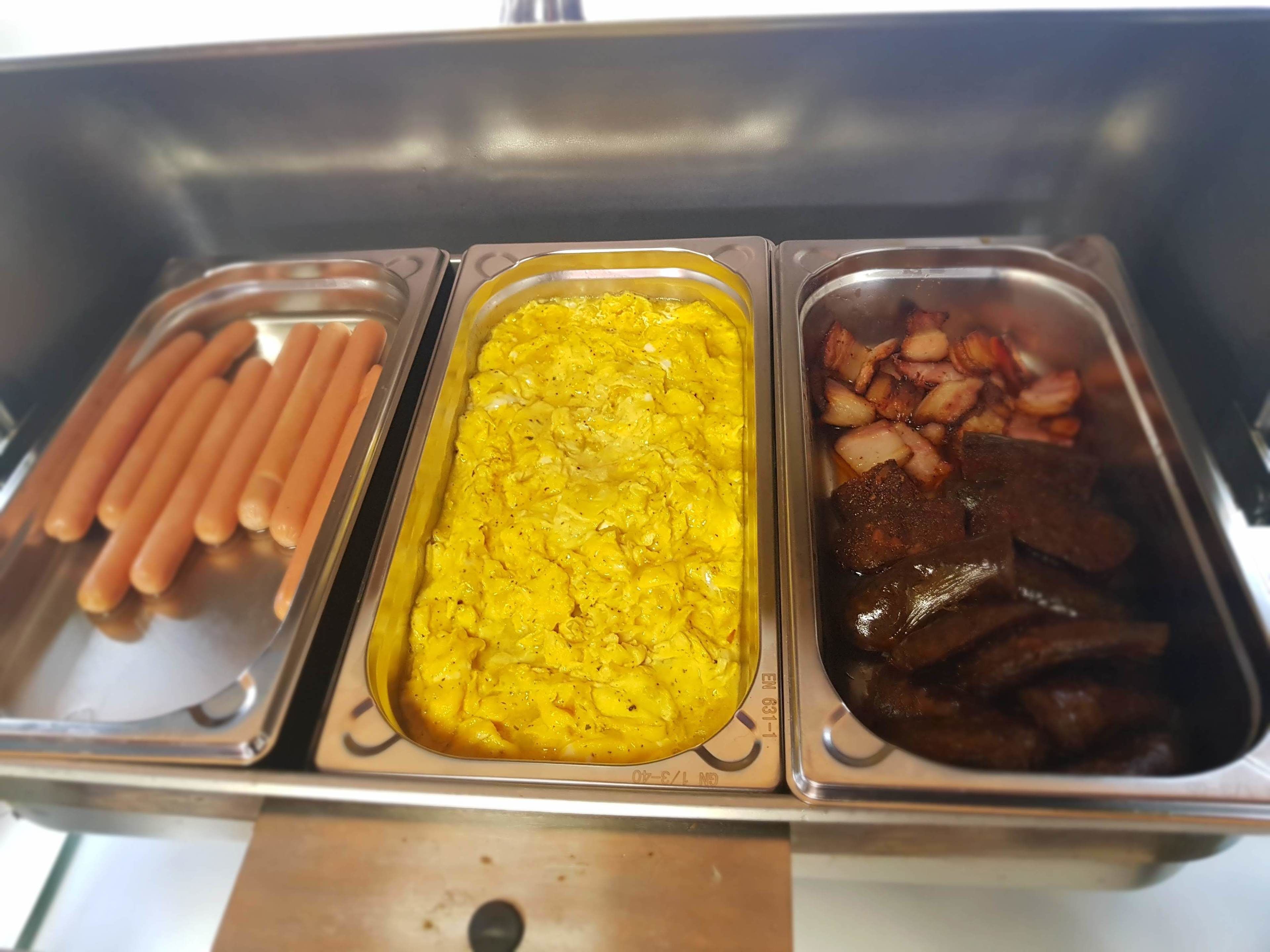 Buffet com cachorros-quentes, ovos mexidos e carnes assadas.