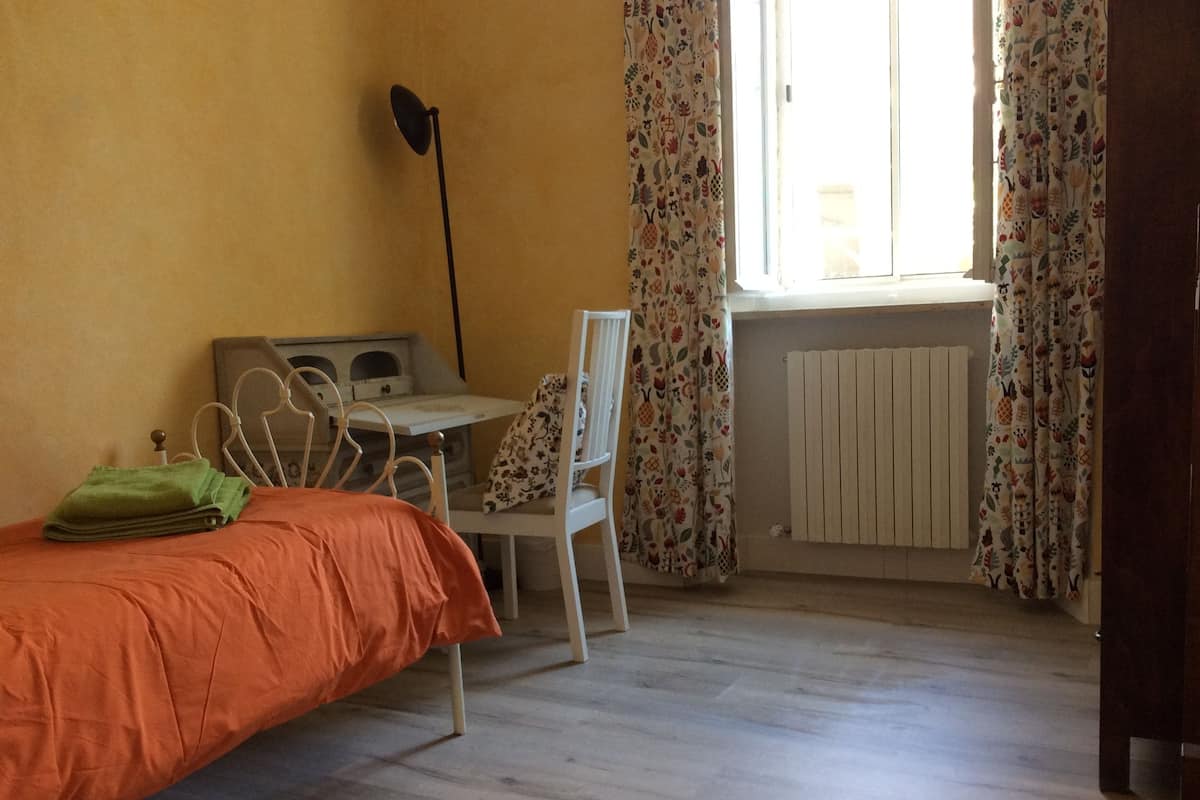 Quarto com cama, escrivaninha, cadeira, radiador e cortinas.