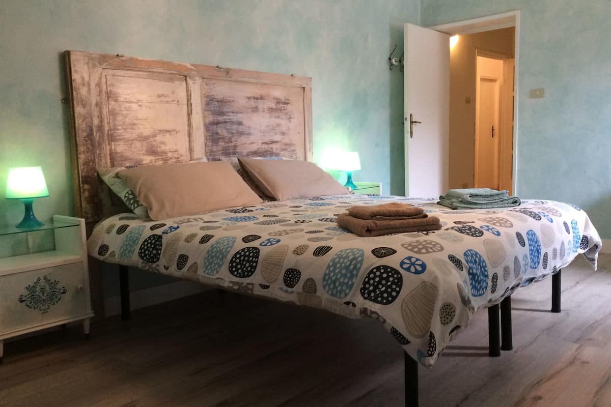 Quarto com cama, duas mesas de cabeceira, um criado-mudo, uma porta e uma parede com textura.