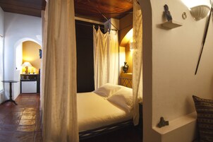 Quarto com cama, mesa de cabeceira, luminária e prateleira na parede.