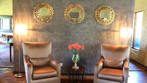 Quarto com duas poltronas, uma mesinha de centro com um vaso de flores e três espelhos fixados na parede.