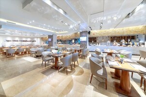 Um restaurante espaçoso com várias mesas e cadeiras, um espaço de bar e um design de teto moderno.