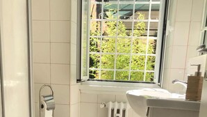 Casa de banho com sanita, lavatório e janela com vista para o exterior verde.