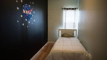 Quarto com parede temática da NASA, uma cama de solteiro e uma janela com cortinas.