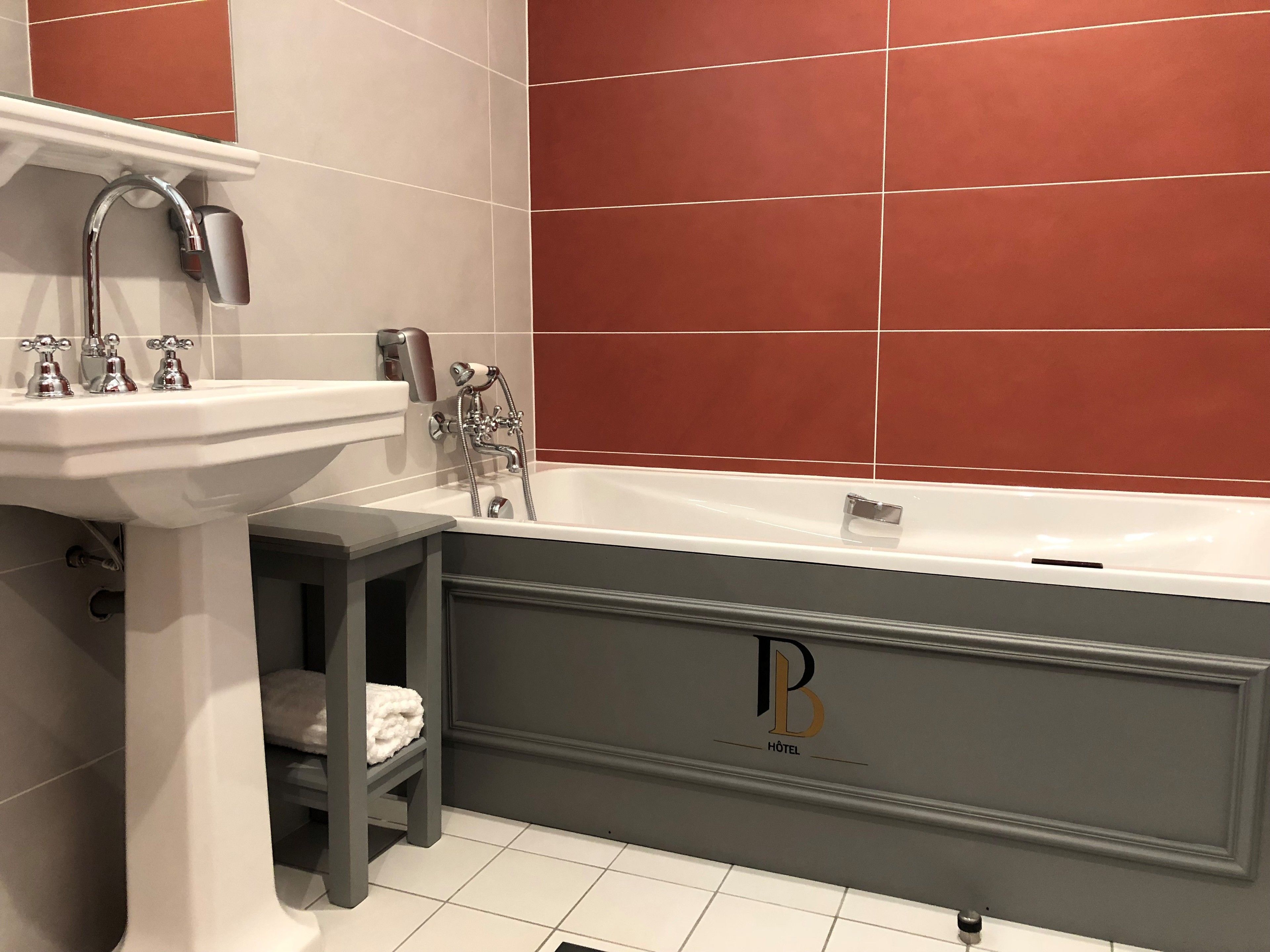 Um banheiro com pia branca, banheira e azulejos vermelhos.