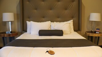 Quarto de hotel com cabeceira estofada, roupa de cama branca e duas mesas de cabeceira com abajures.