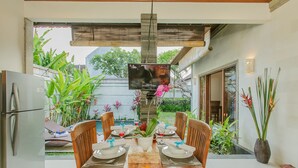 Uma sala de jantar com uma mesa de madeira posta para quatro pessoas, rodeada por cadeiras, e uma televisão montada acima.