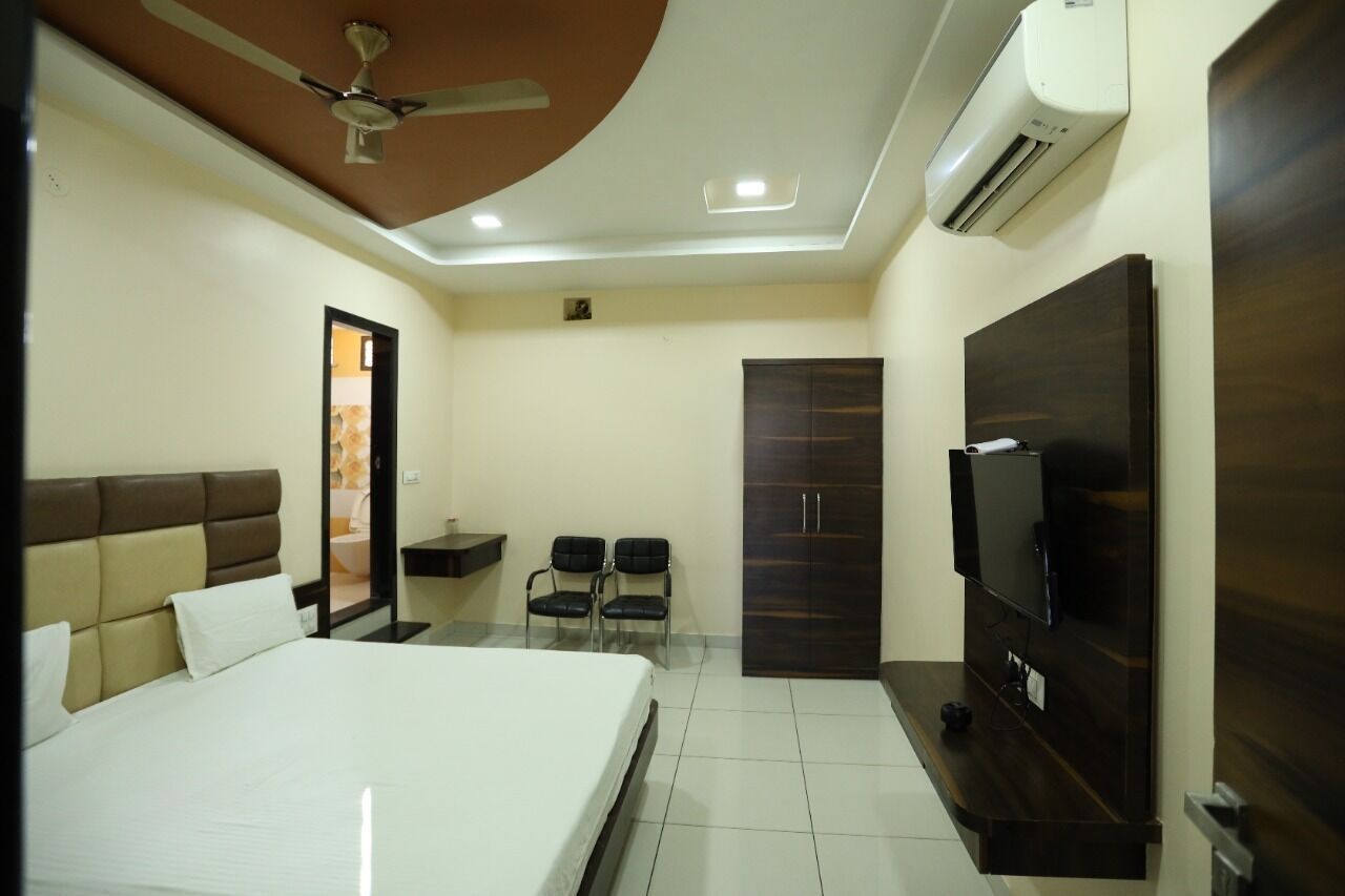 Quarto de hotel com cama, televisão, guarda-roupa, escrivaninha e ventoinha no teto.