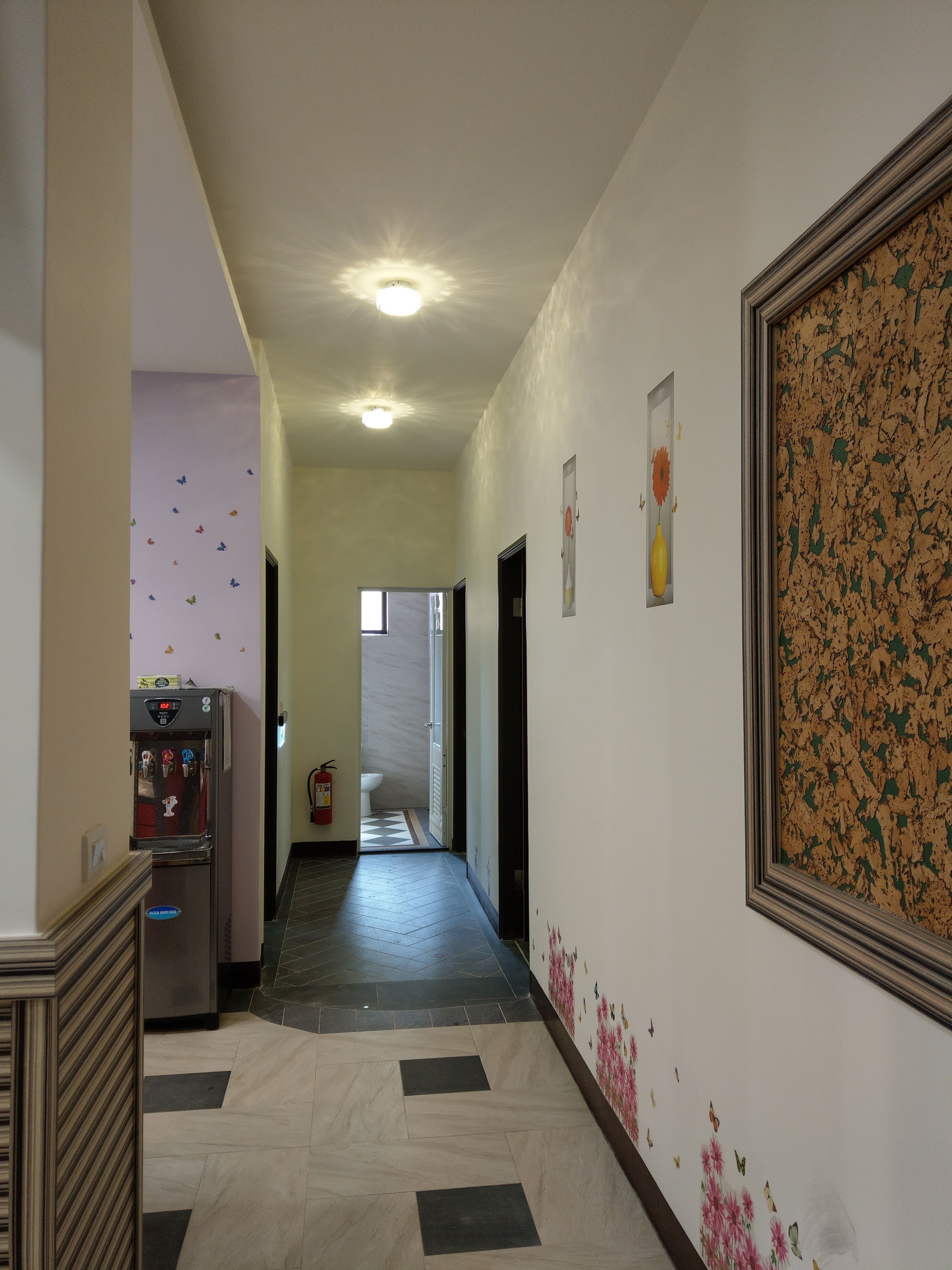 Corredor com geladeira, extintor de incêndio e porta de acesso a um banheiro.