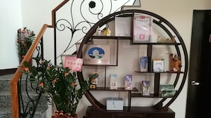 Uma área de recepção com escada de madeira, planta decorativa, um expositor circular com certificados e um armário de madeira com gavetas.