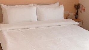 Cama bem arrumada com lençóis brancos em quarto com paredes cor de pêssego e piso de madeira.