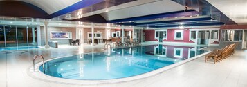 Piscina interna com vista para a área da piscina, cadeiras de descanso e um balcão de recepção.