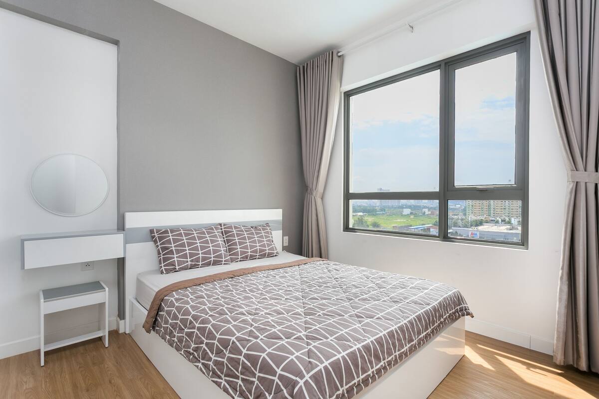 Quarto moderno com uma cama grande, uma mesa de cabeceira, um espelho redondo e uma janela com cortinas.