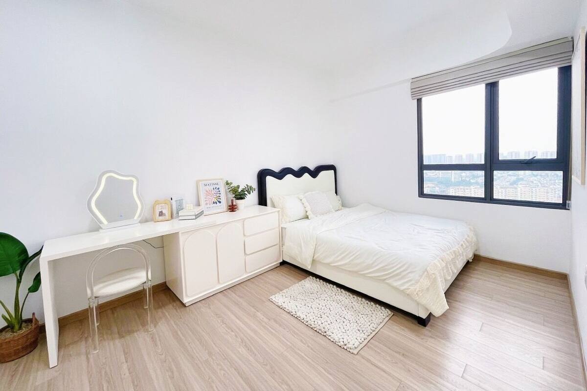 Quarto com cama, escrivaninha com cadeira, cómoda, espelho, janela e planta.