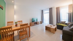 Uma sala de estar moderna com uma mesa de jantar de madeira, cadeiras, uma TV, um sofá e uma mesa de centro.
